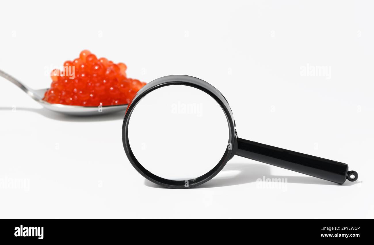 Magnifying glass and spoon with red caviar on a white background Stock ...