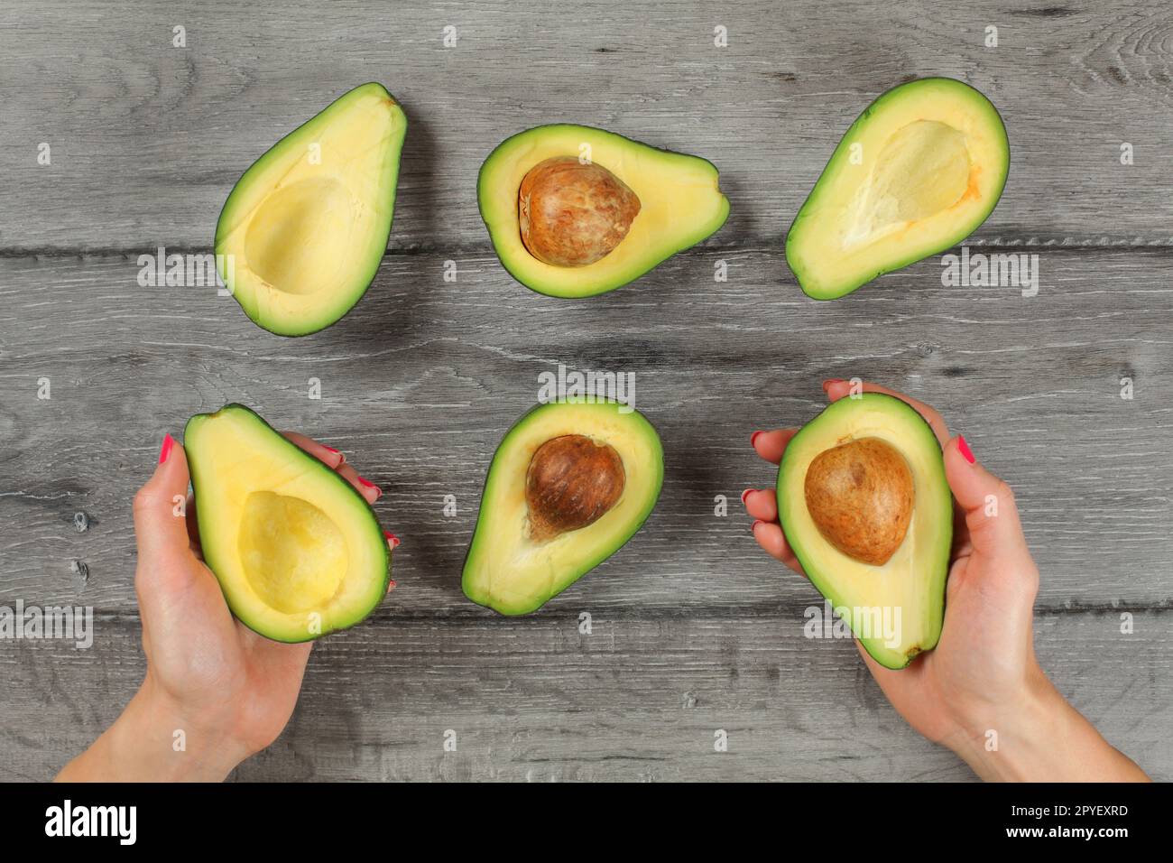 Tabletop view, woman hands holding avocado cut in half, seed visible ...