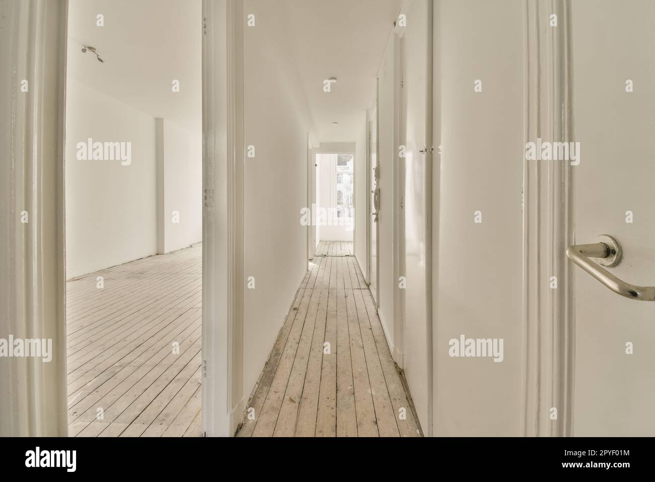 a long hallway with white walls and wood flooring on either side by ...