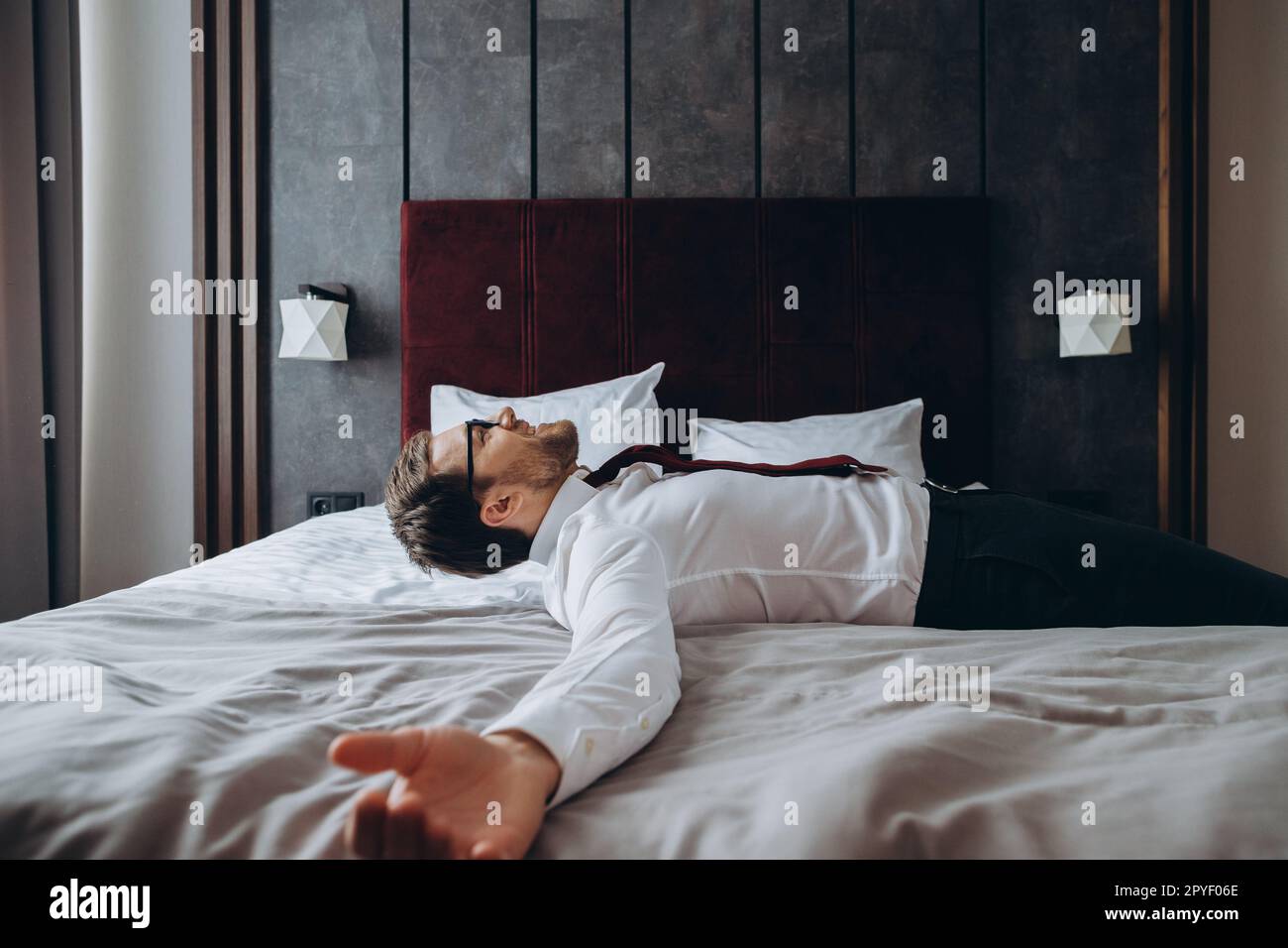 Exhausted businessman resting on bed after long air flight, jet lag. Man in business suit lying ...