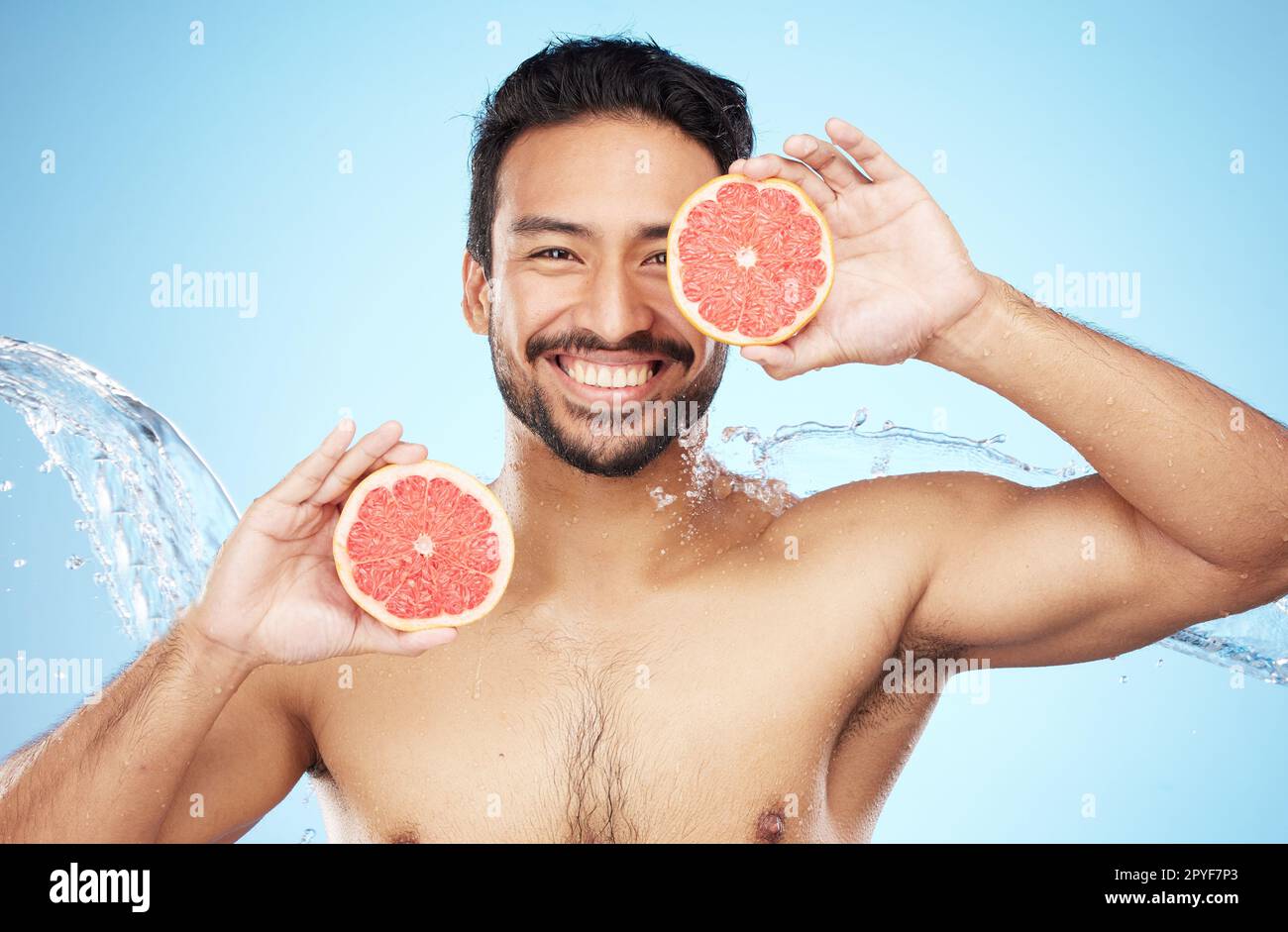 Face, water and grapefruit with a man model in studio on a blue background for hygiene or ...