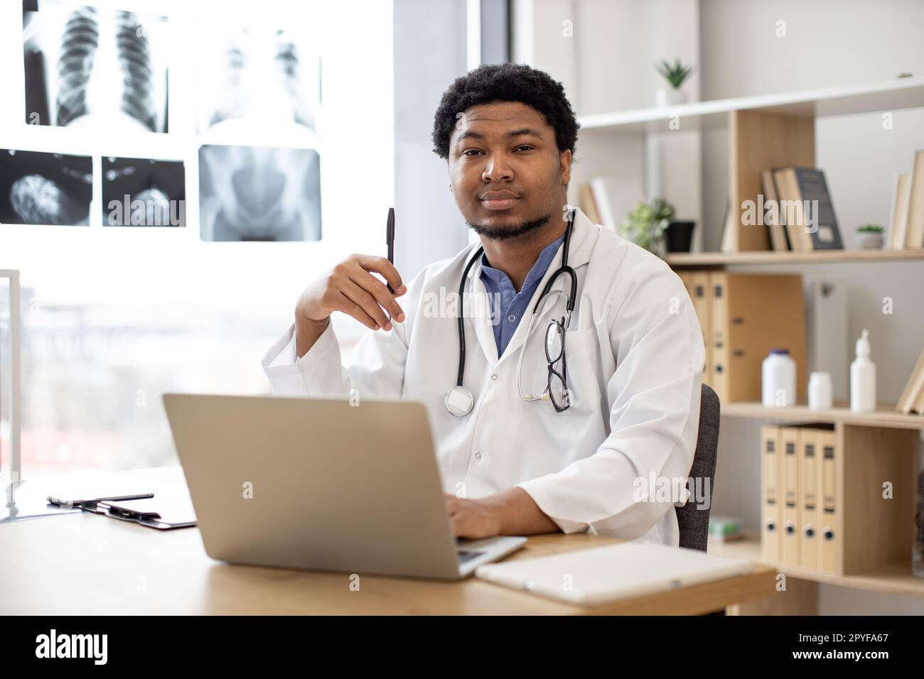 Pensive multiethnic male therapist in white coat posing with pen in ...