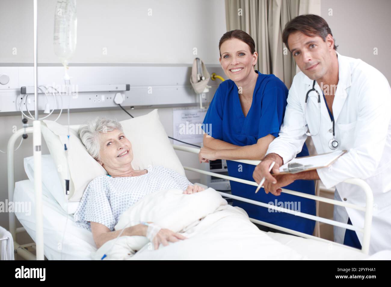 Happy patient. Portrait of a doctor and his nurse standing over their patients bed Stock Photo ...