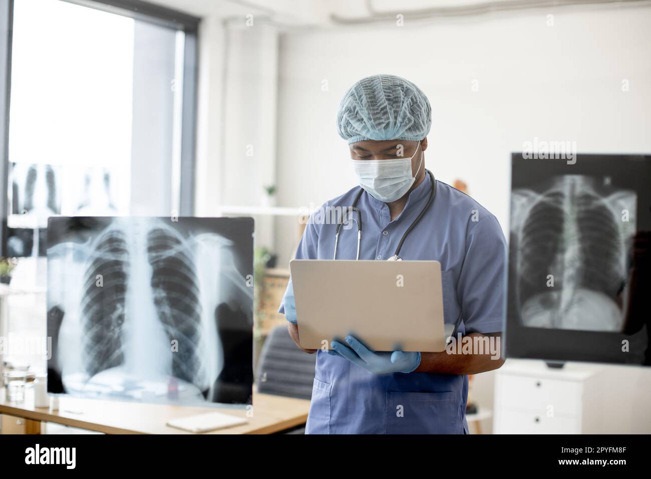 Mindful african american man in scrubs, mask and medical cap examining ...