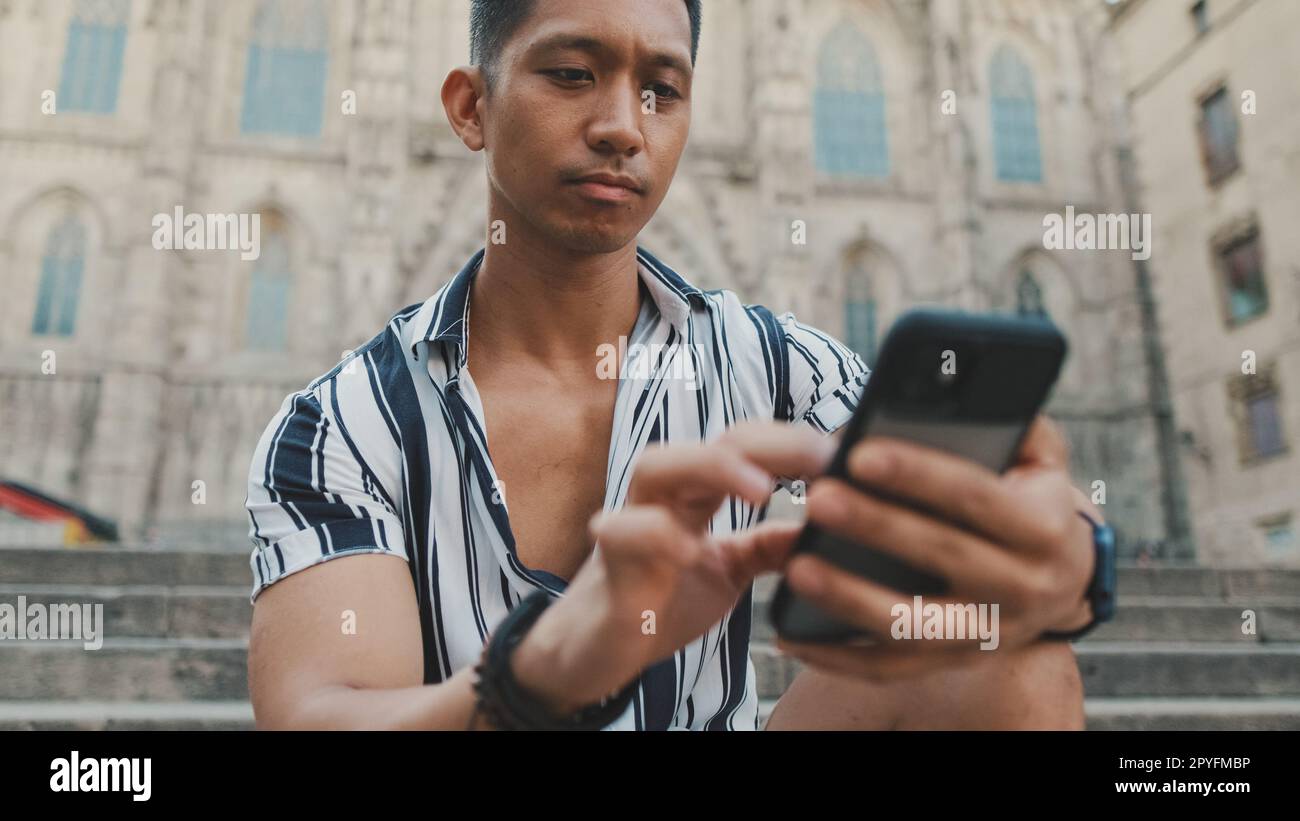 Young man tourist on steps uses mobile phone while sitting on landmarks ...