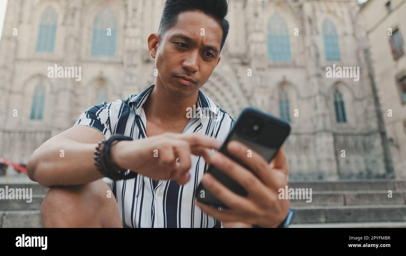 Young man tourist on steps uses mobile phone while sitting on landmarks ...