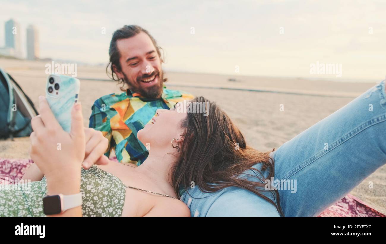 Young couple relaxing on the beach, talking, using mobile phone Stock ...
