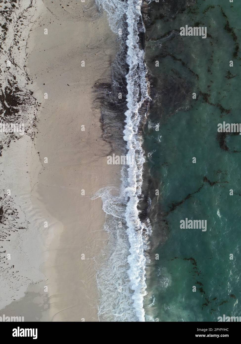 An aerial shot of a beach, featuring rocks and crystal-clear blue water ...