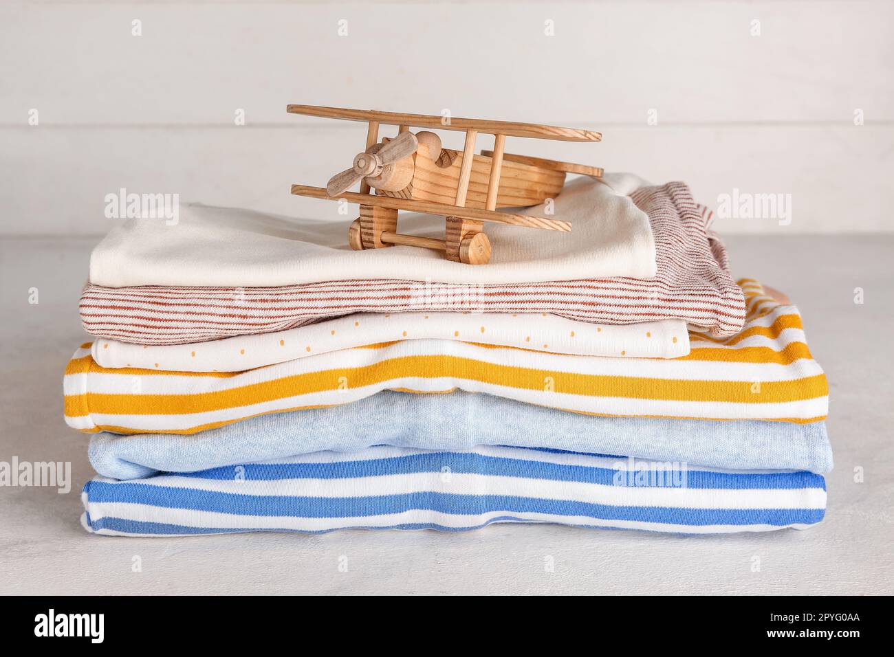 Stack of baby clothes and wooden toy on light table Stock Photo - Alamy