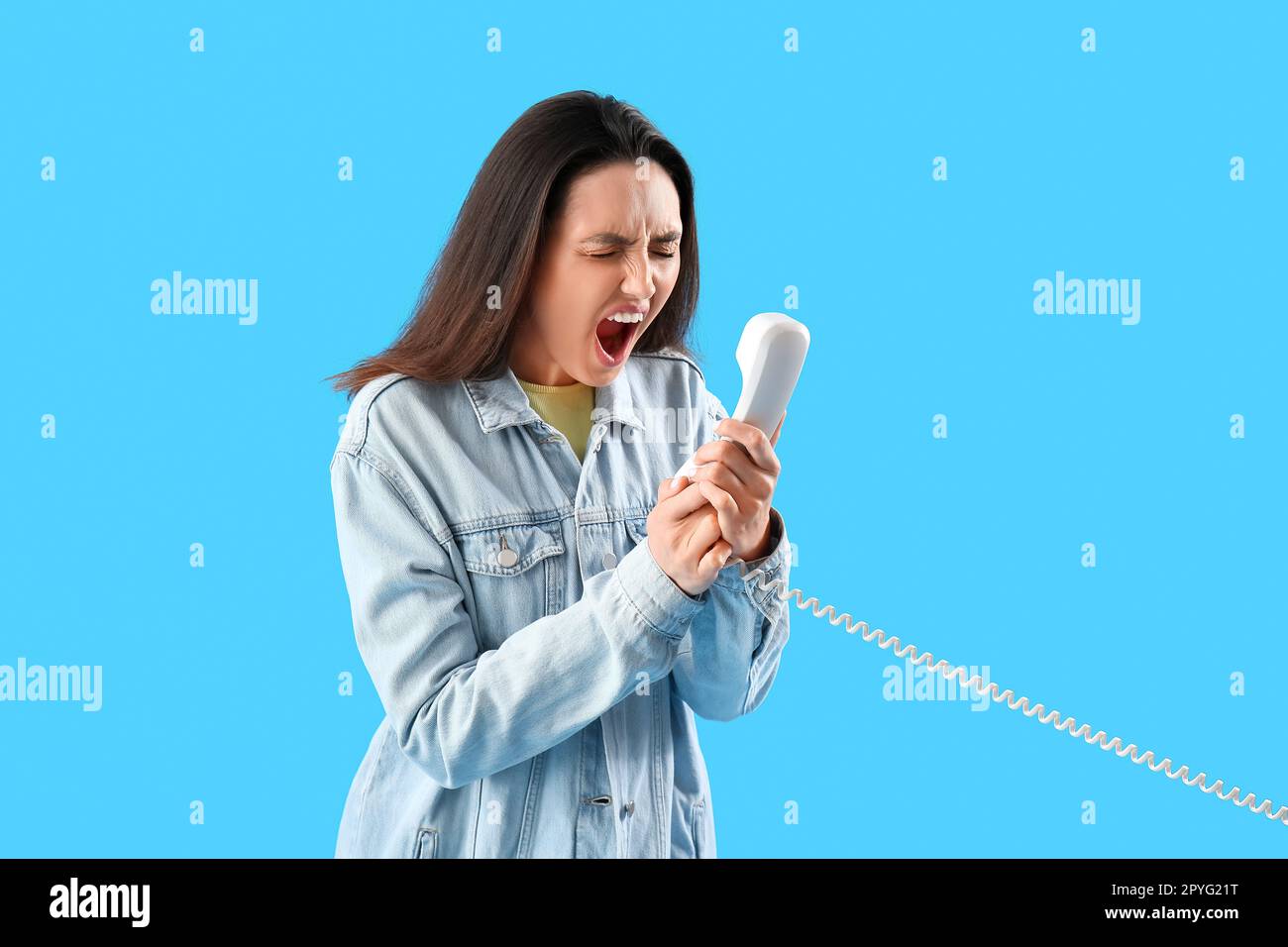 Angry screaming young woman with telephone receiver on light blue ...