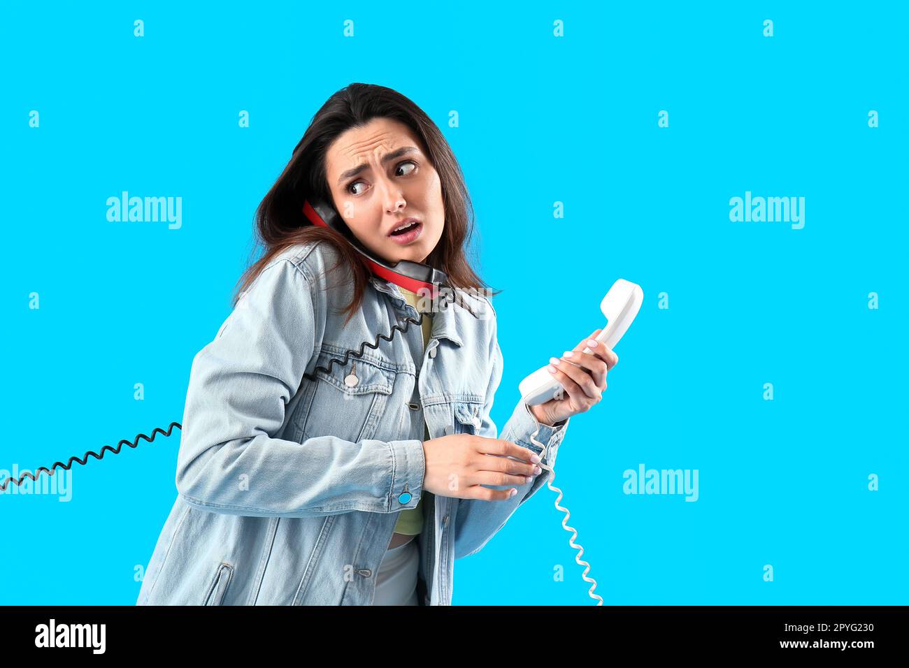 Sad young woman with telephone receivers on light blue background Stock ...