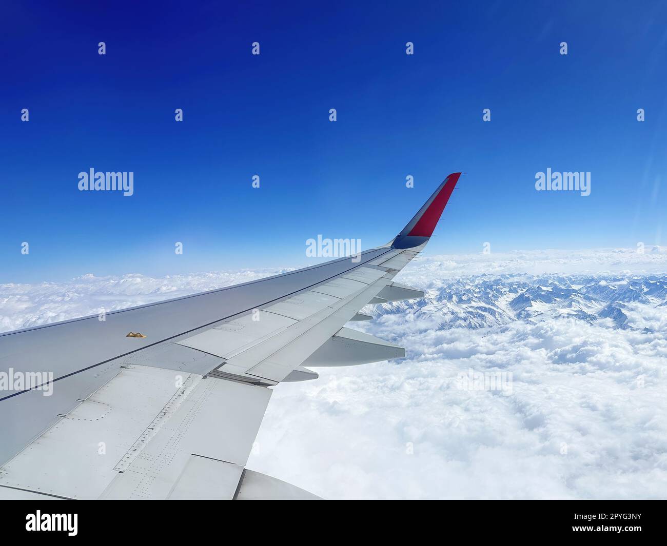 Wide airplane wing high up over the big snowy mountains range. Air ...