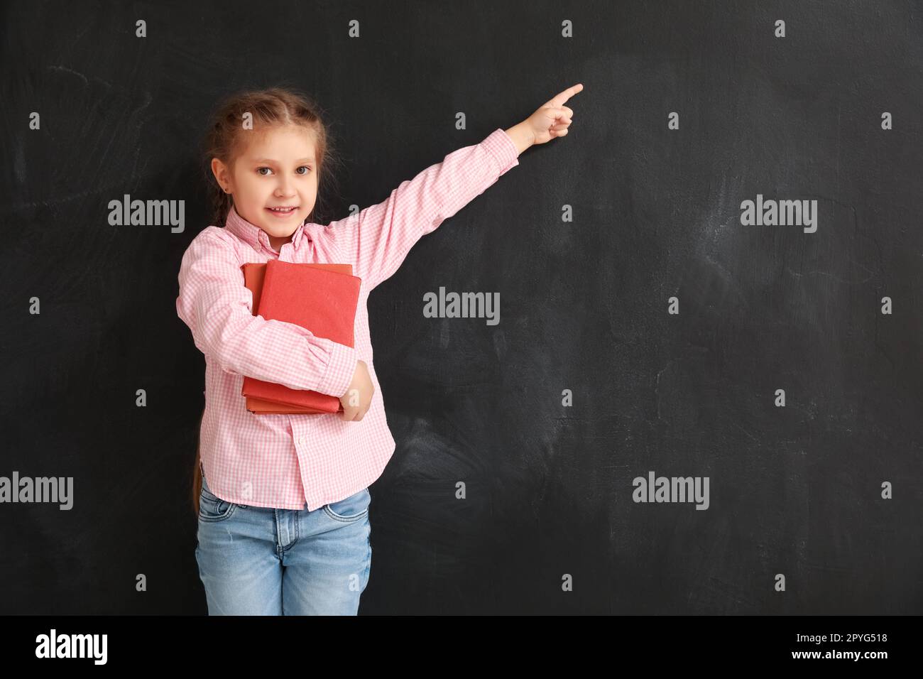 Little girl with books pointing at blackboard. Children's Day ...