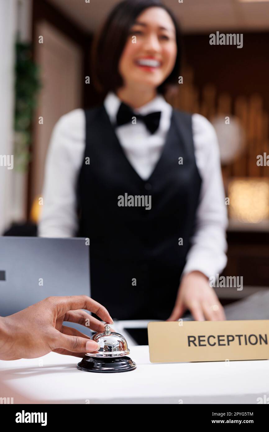 Person ringing bell at hotel reception with front desk staff working on ...
