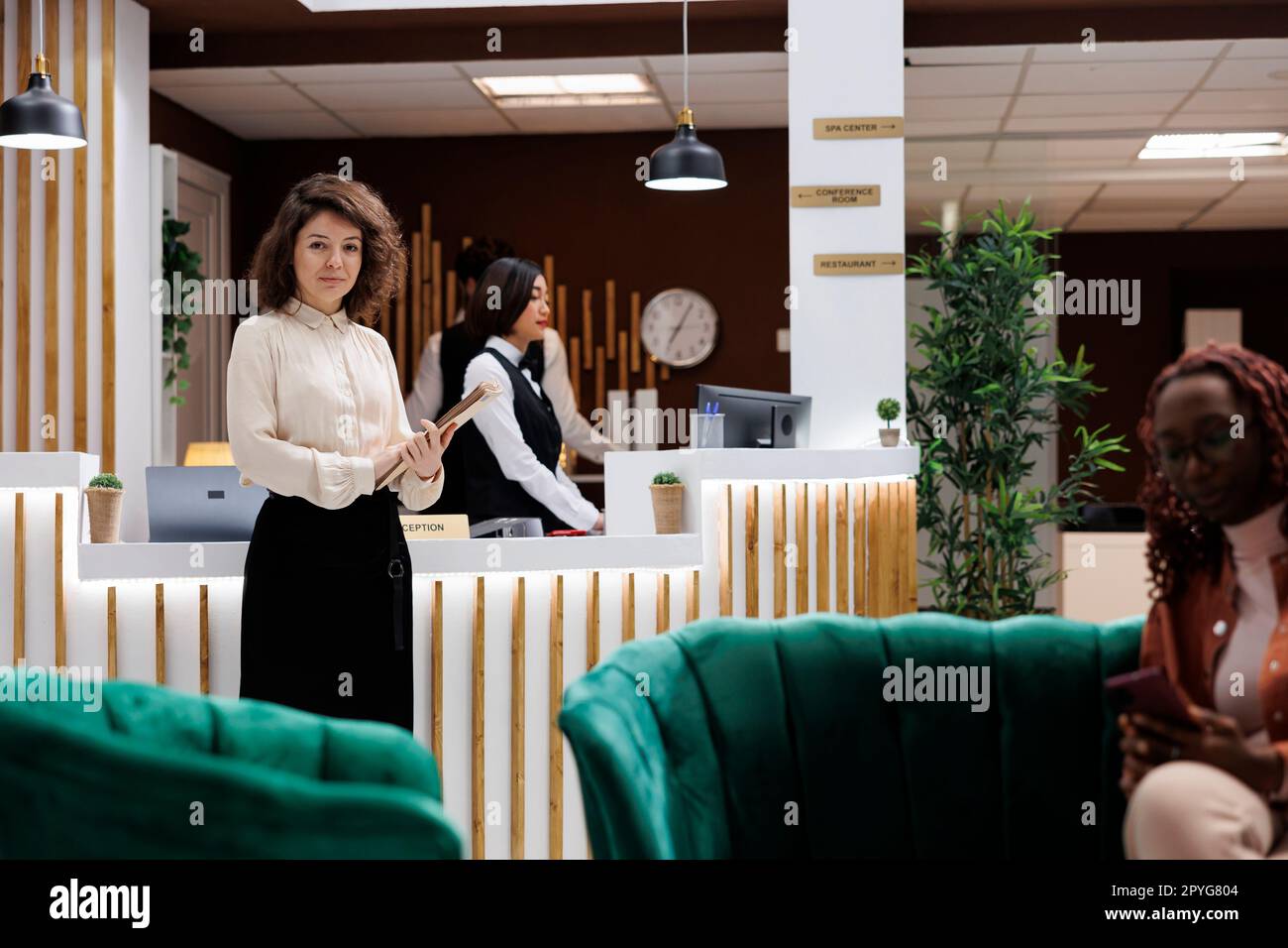 Portrait of hotel manager with records standing in reception desk lobby ...