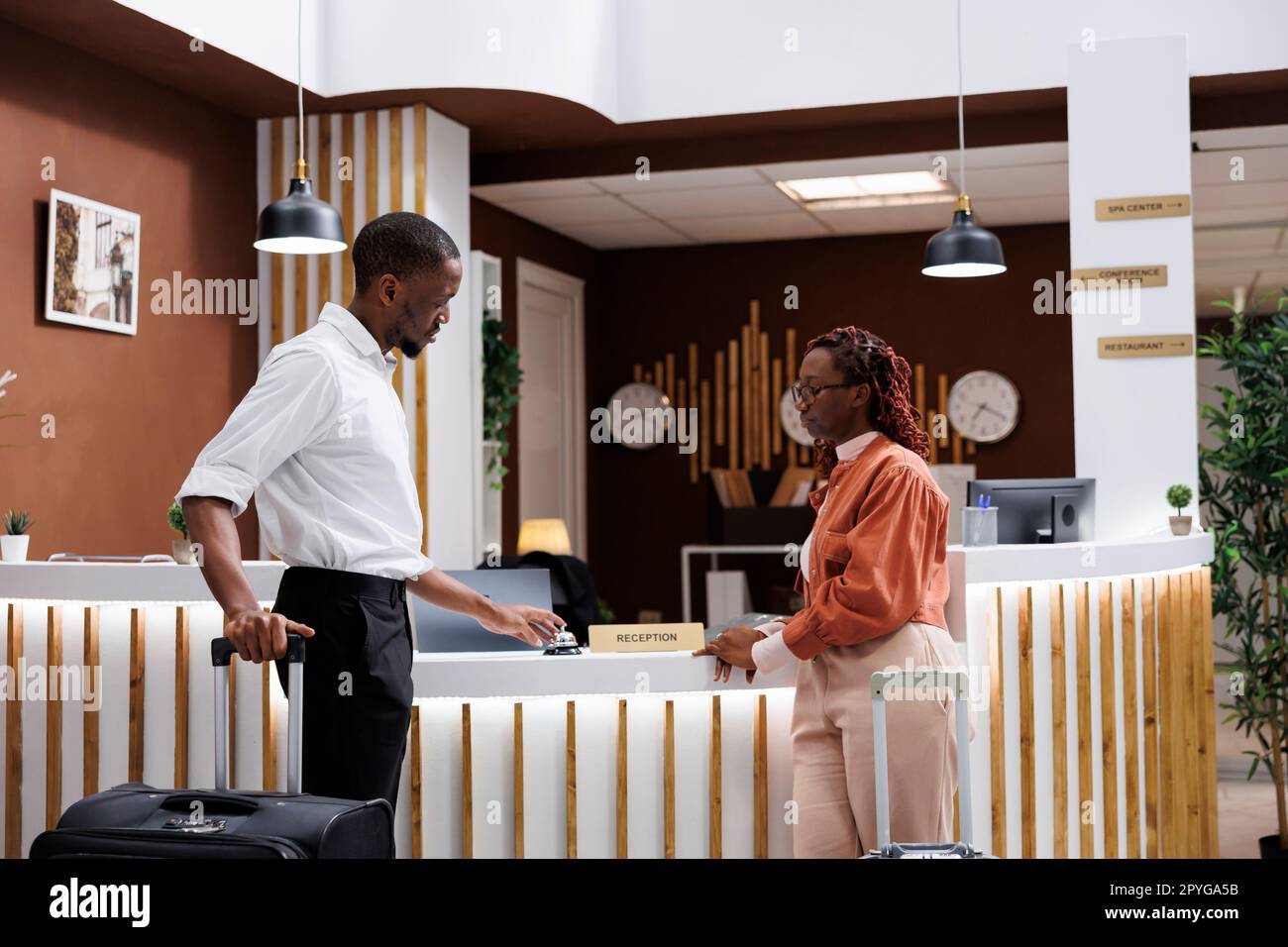 Two people waiting to check in at hotel, standing near reception desk ...