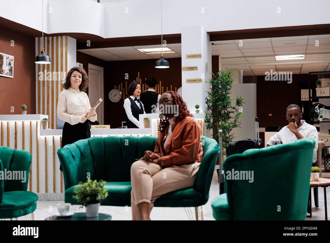 Hotel manager with employees and guests in lounge area and lobby ...