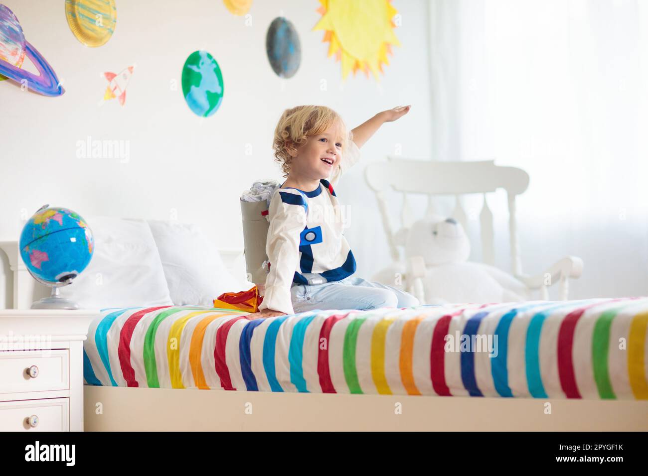 Kids play astronaut. Little boy in space costume jumping on bed with ...