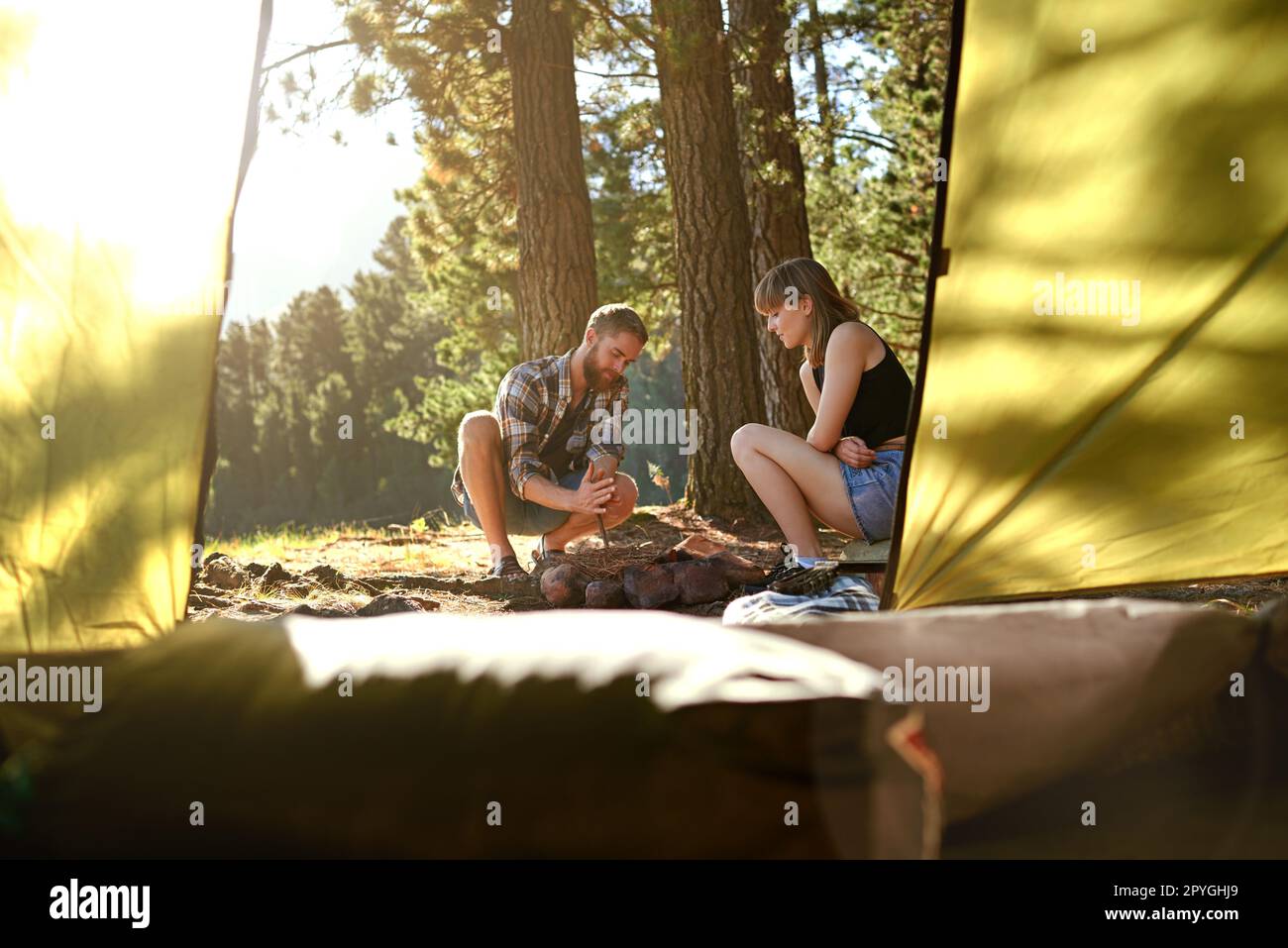 Into the woods. a young couple starting a fire by hand while camping ...