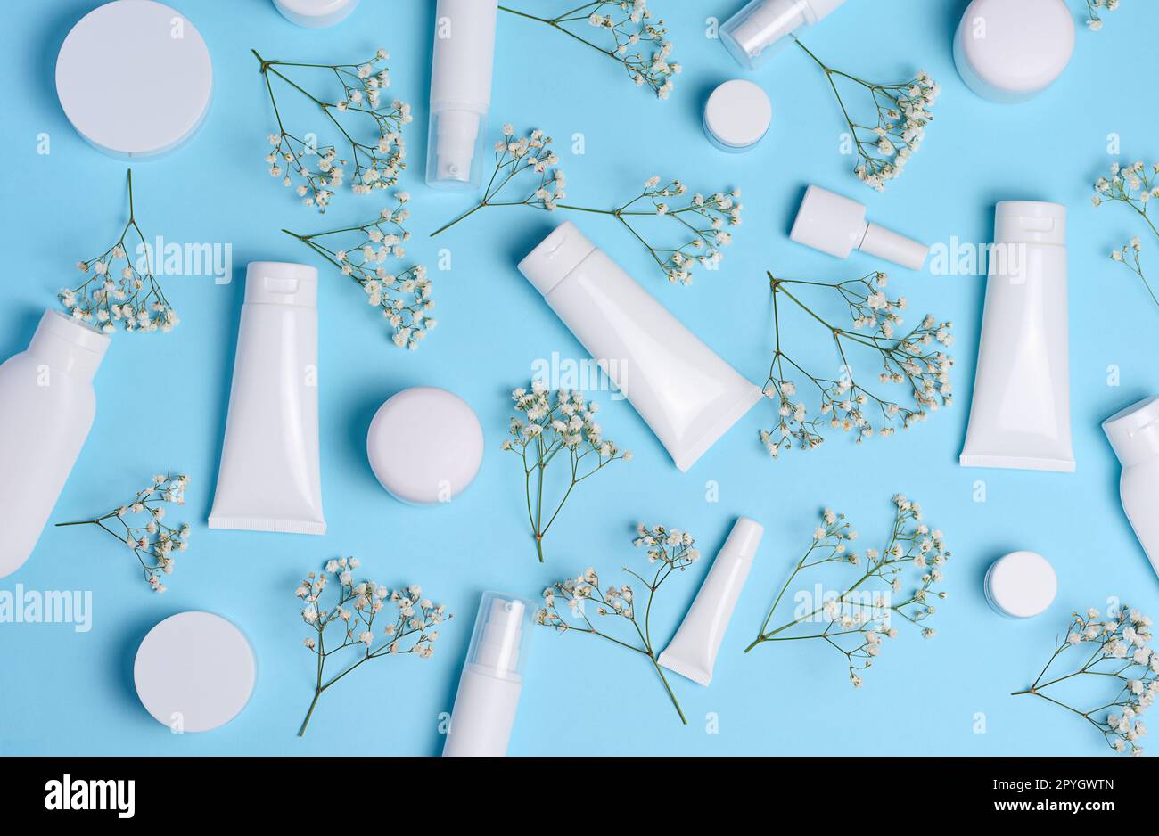 White plastic tubes, jars, and gypsophila branches on a blue background ...