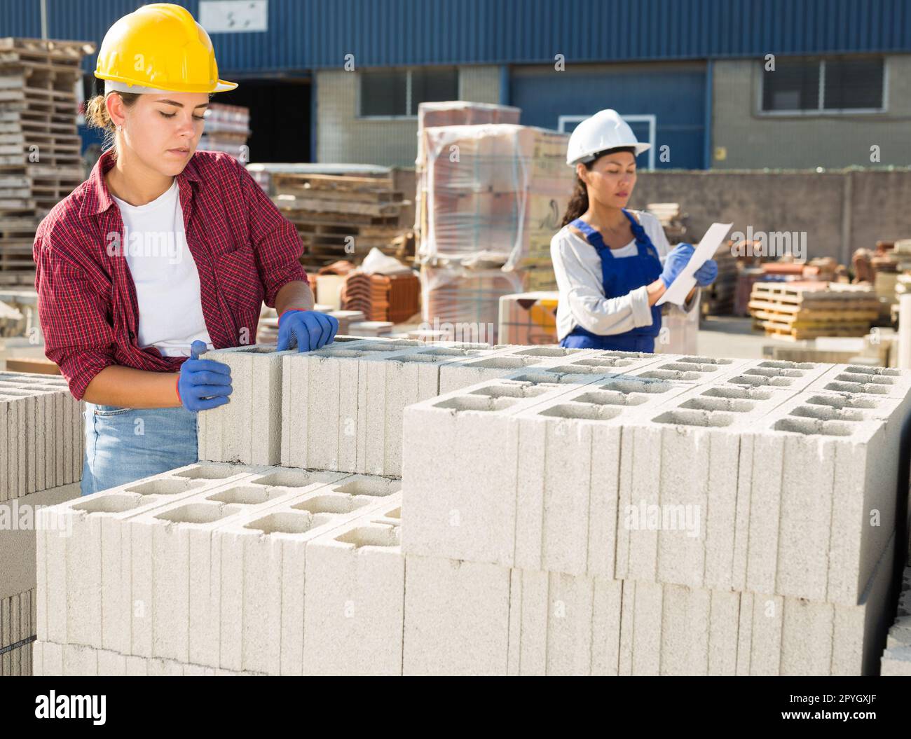 Worker stacking bricks in warehouse of building materials on an open ...
