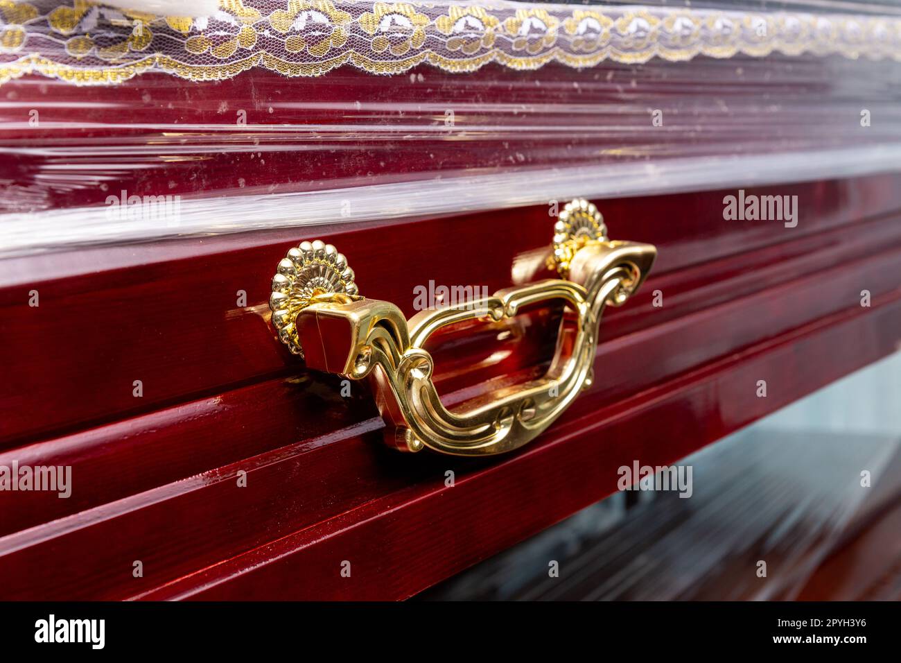 New wooden coffin with a handle made of yellow metal, packed in plastic ...