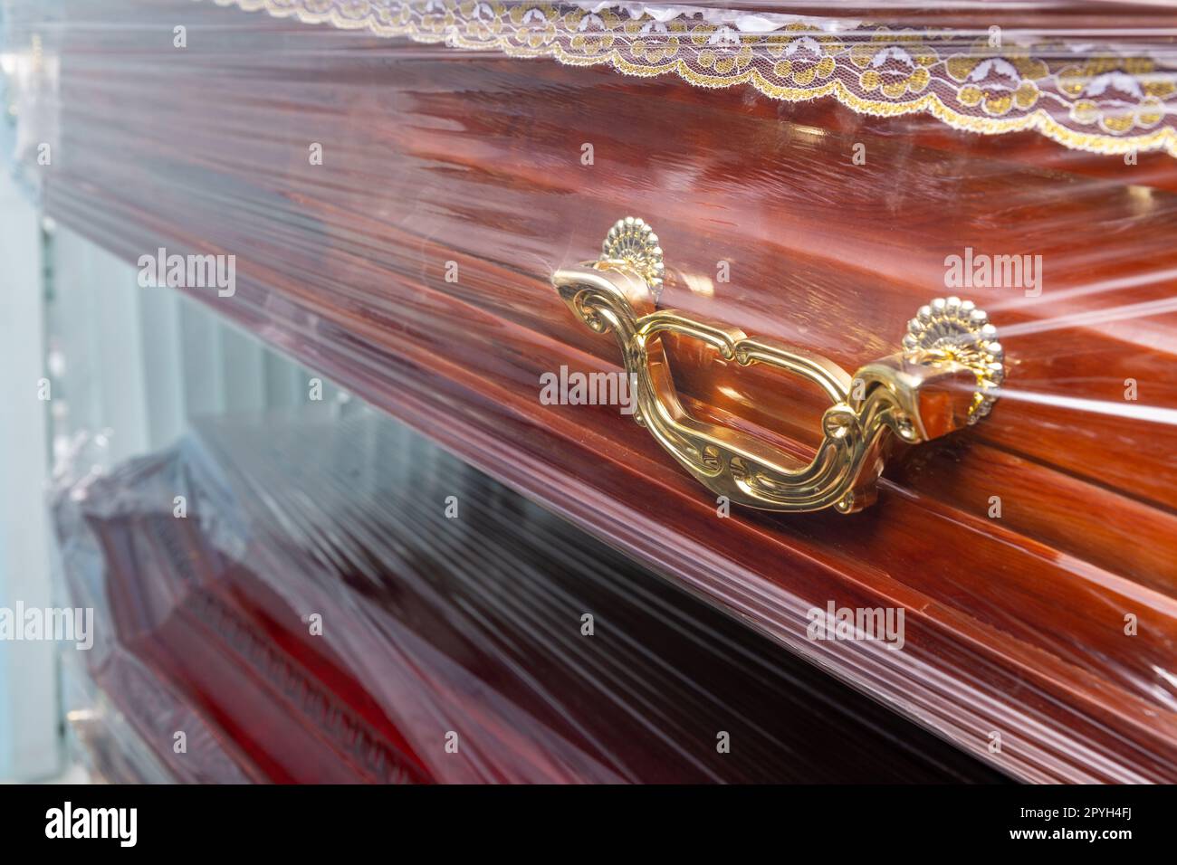 New wooden coffin with a handle made of yellow metal, packed in plastic ...
