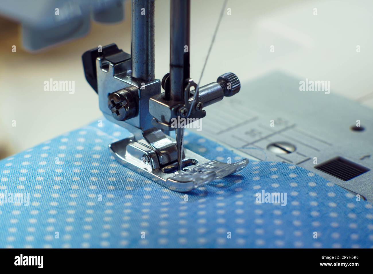 Macro shot of sewing machine steel pressure foot with needle and thread ...