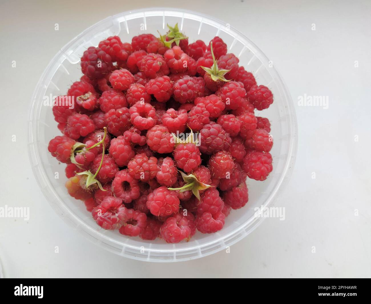 Red juicy raspberries in plastic box container on white background, top ...