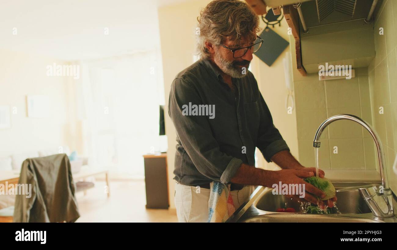Elderly positive man washing vegetables in the kitchen Stock Photo - Alamy