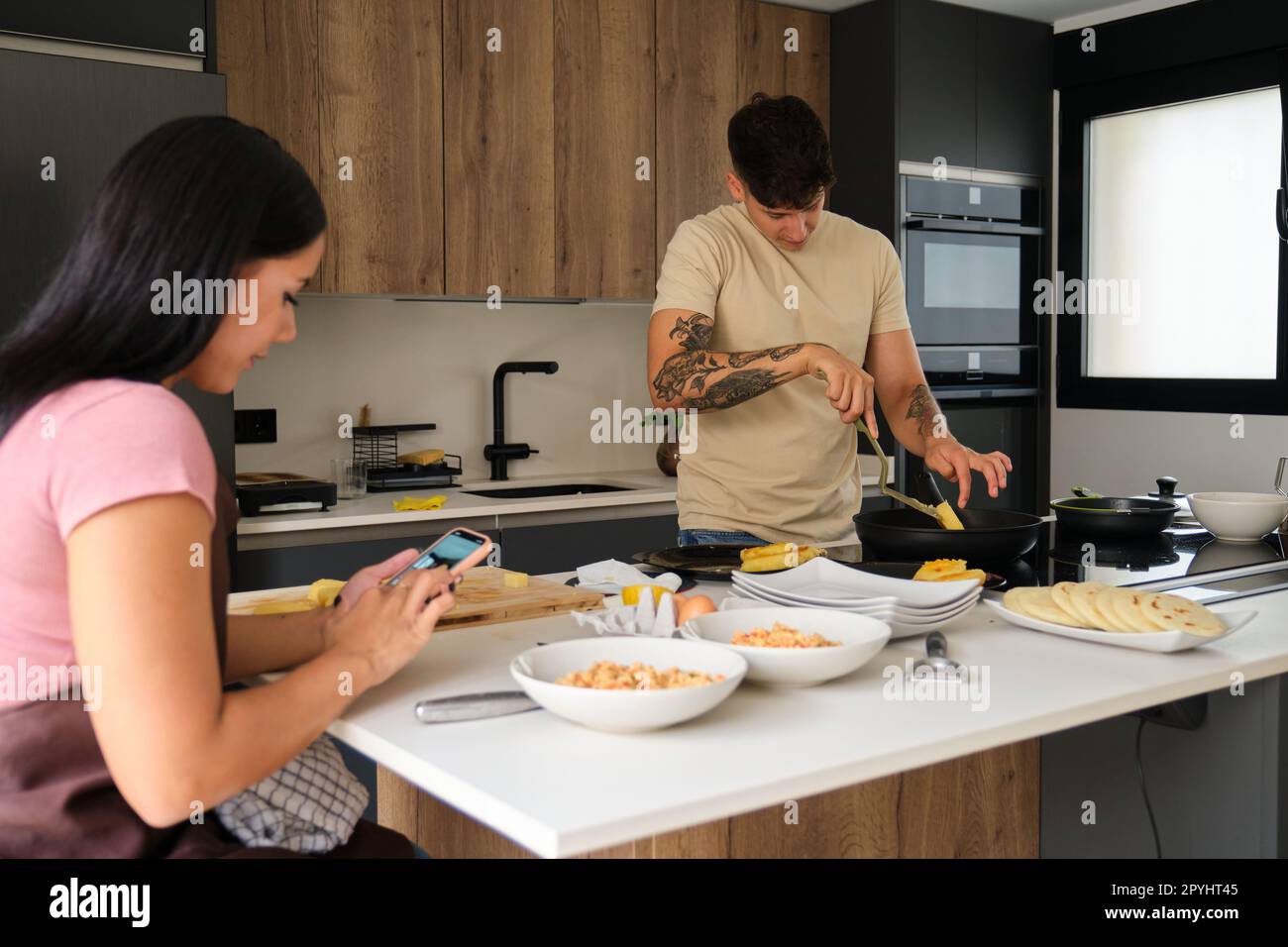 Two young latin people using the phone while cooking Stock Photo - Alamy