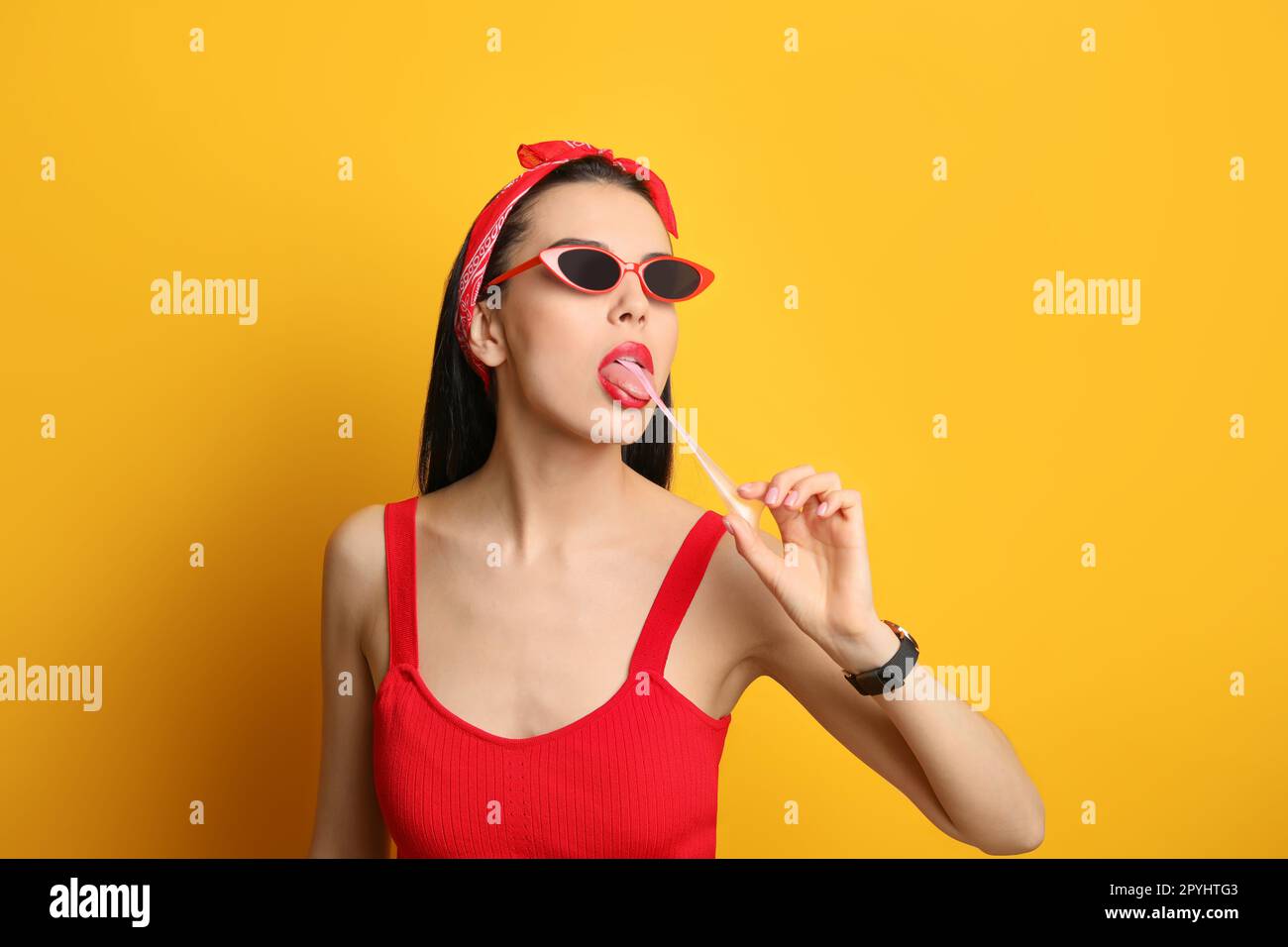 Fashionable young woman in pin up outfit chewing bubblegum on yellow ...