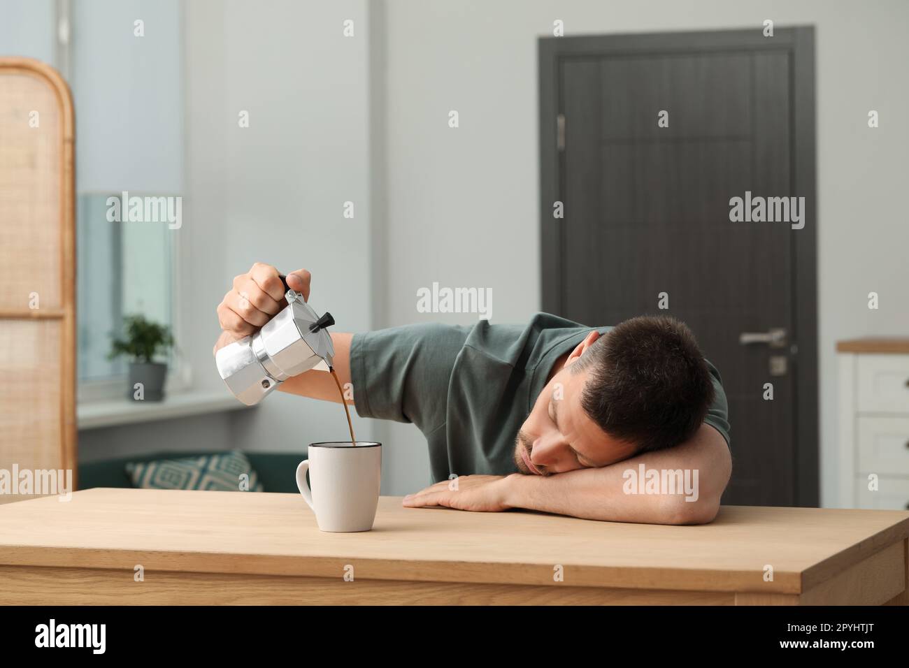 Sleepy man pouring coffee in cup at wooden table indoors Stock Photo ...