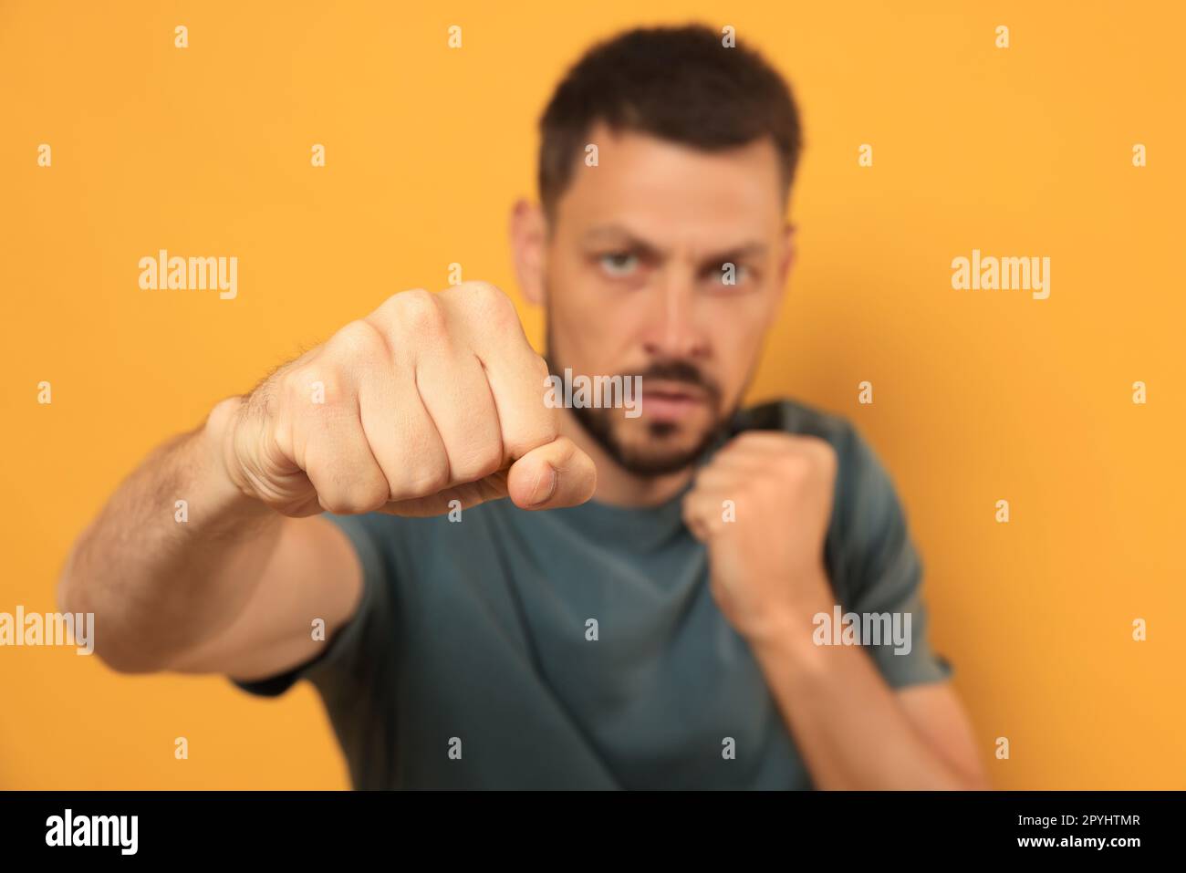 Man throwing punch against orange background, focus on fist. Space for ...