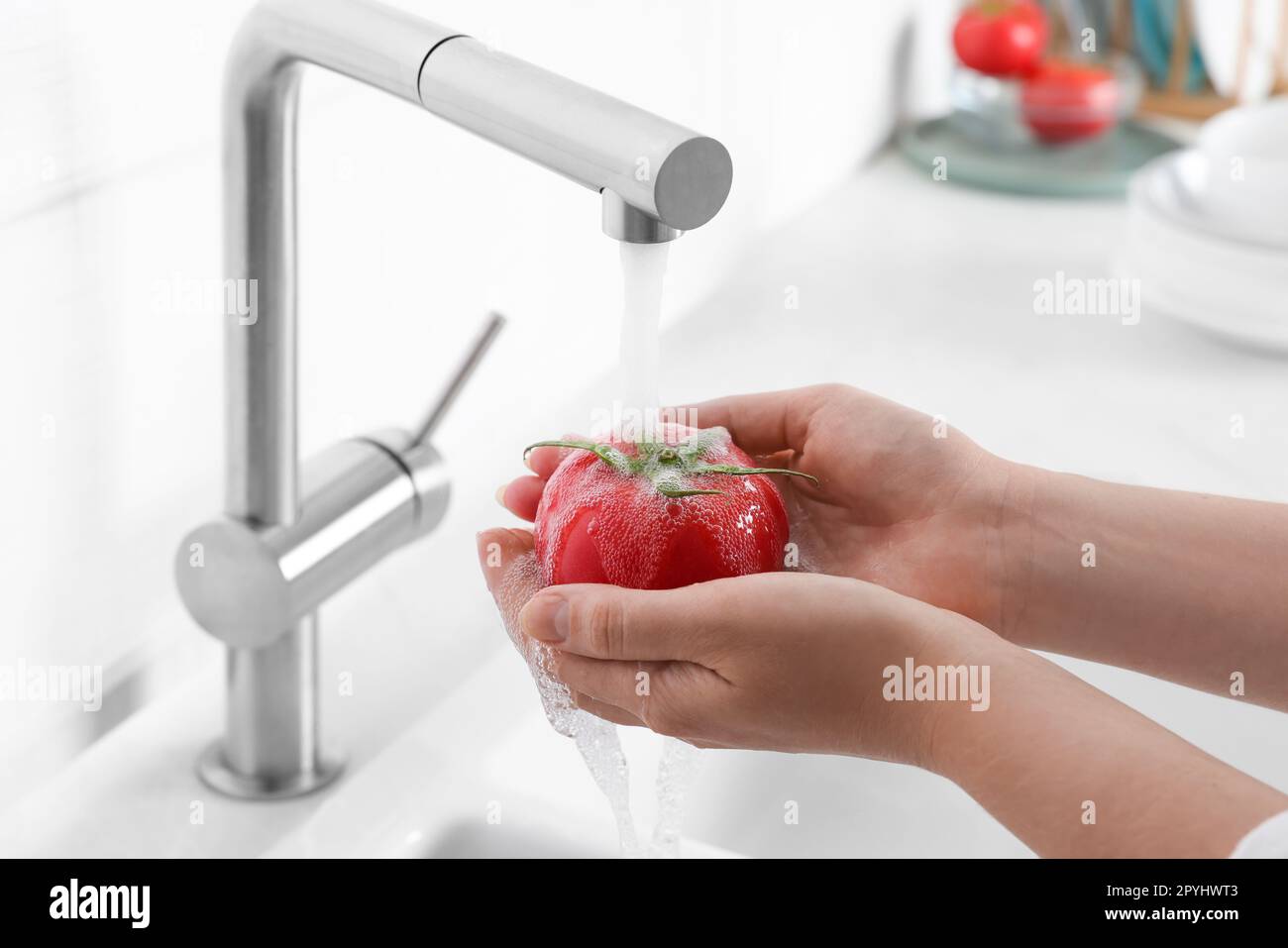 Woman washing fresh ripe tomato under tap water in kitchen, closeup ...