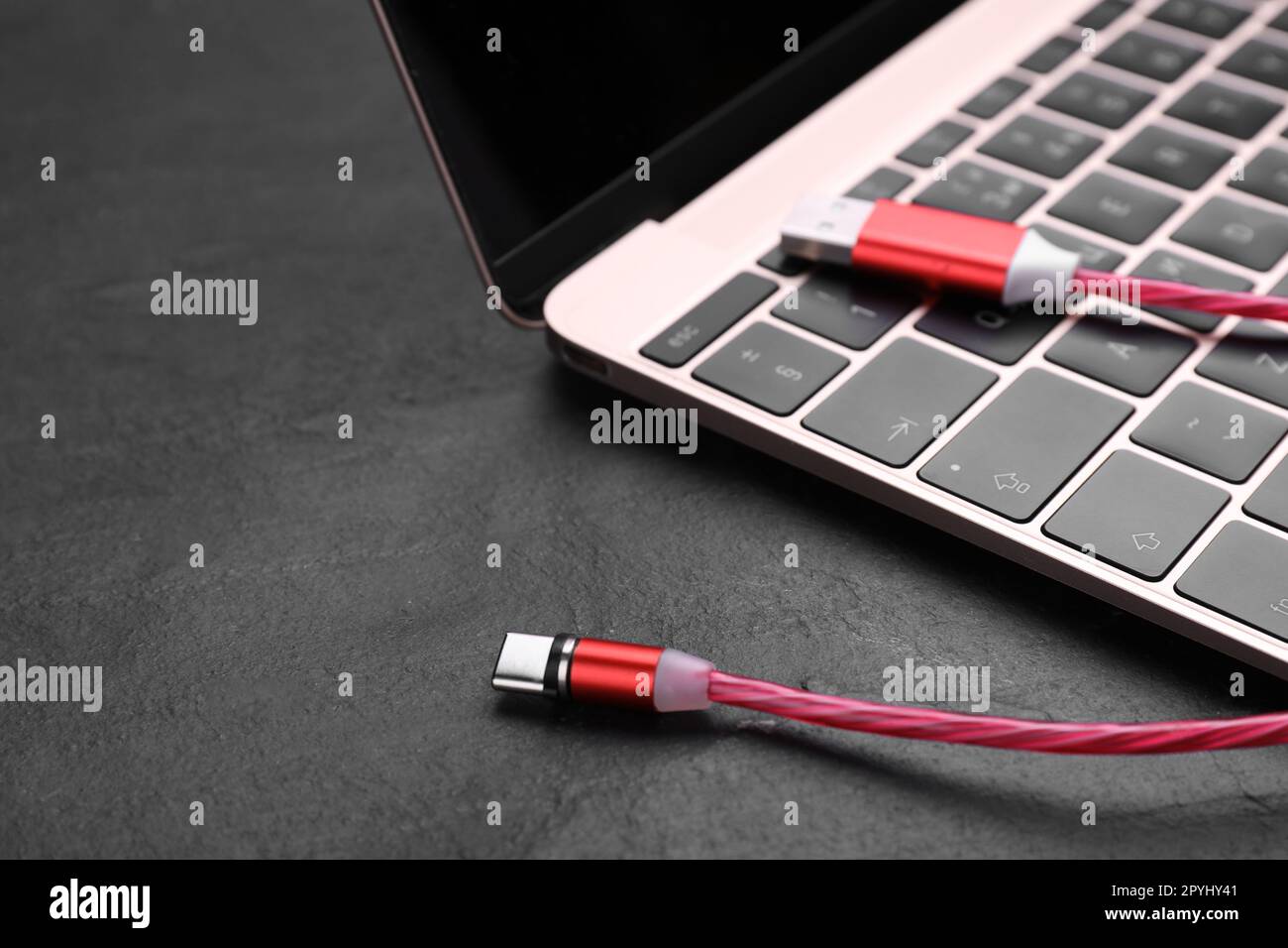 Red USB cable with type C connector and laptop on black slate table ...