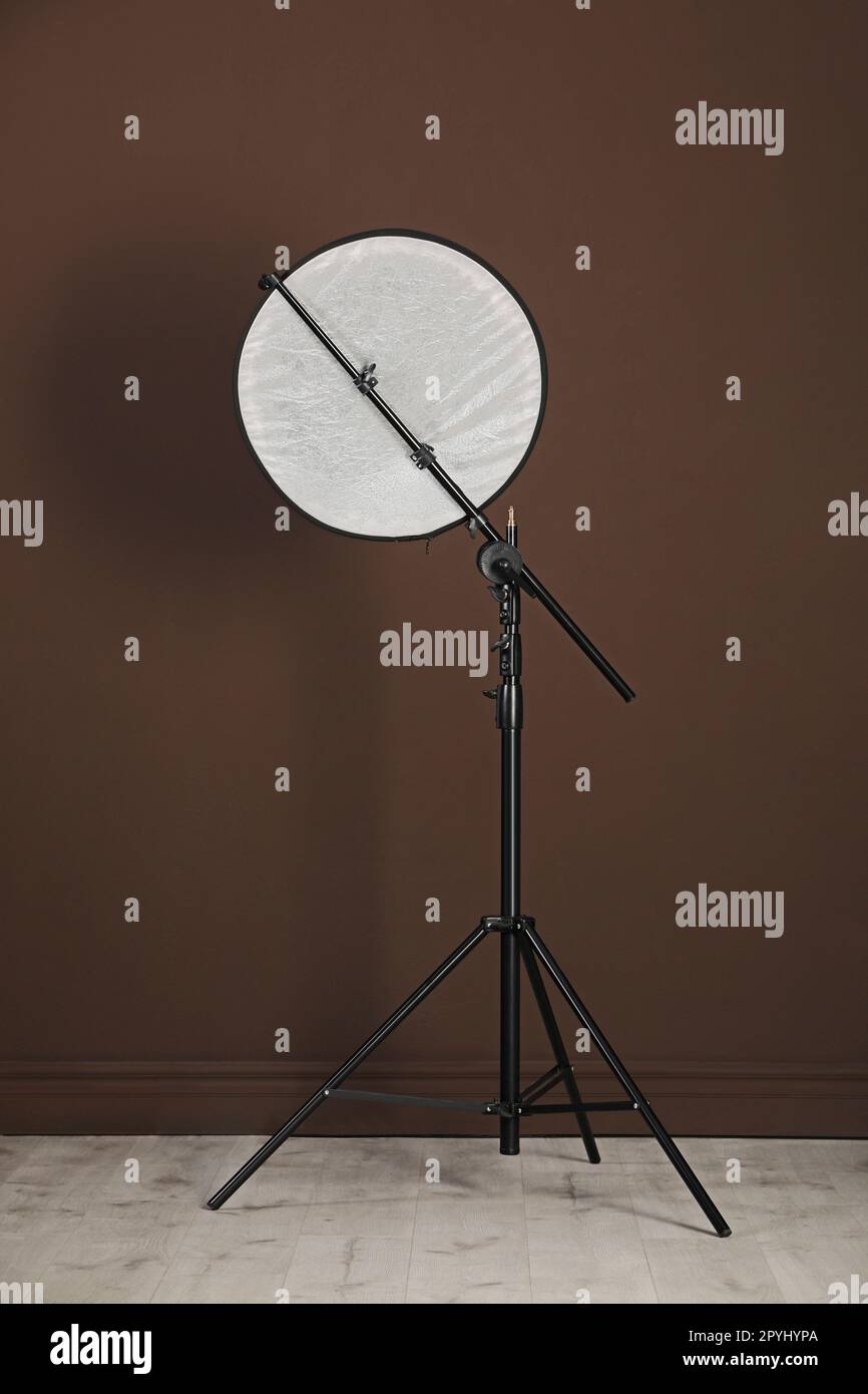 Studio reflector on tripod near brown wall indoors. Professional ...
