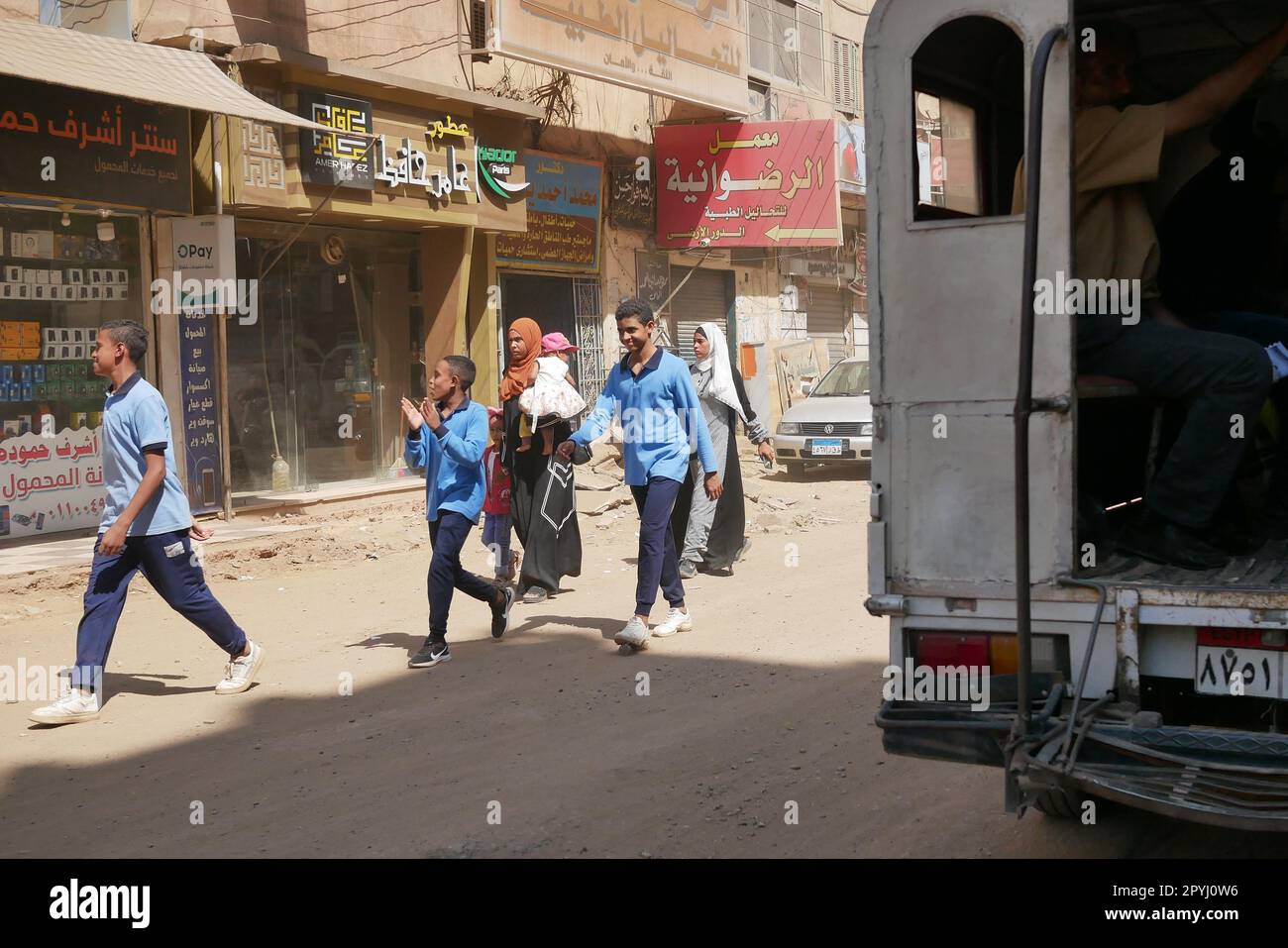 People walking past a public minivan on the dusty streets of Al-Balyana ...