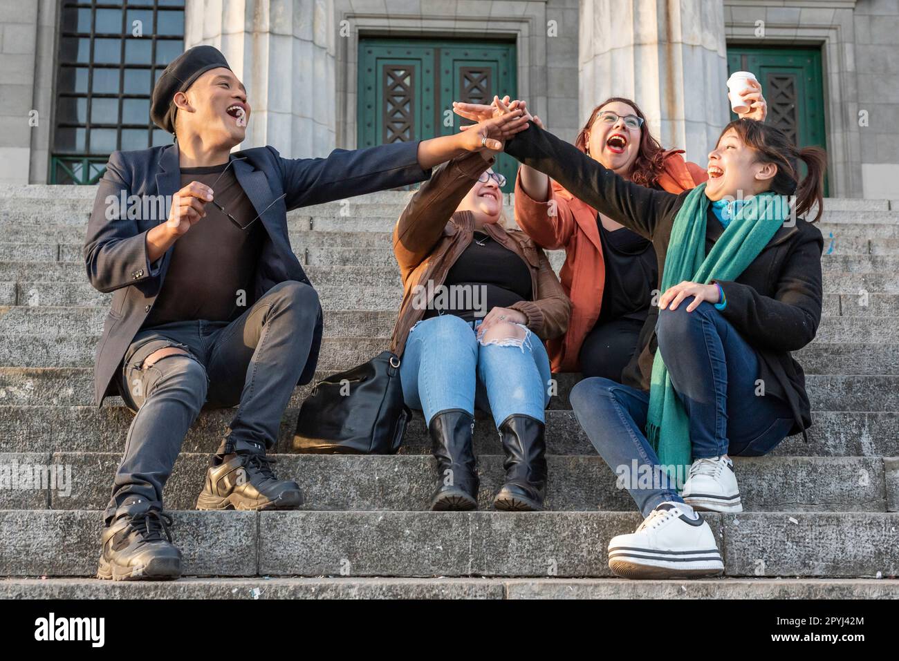 A group of friends laughing and doing high five while sitting on stairs ...