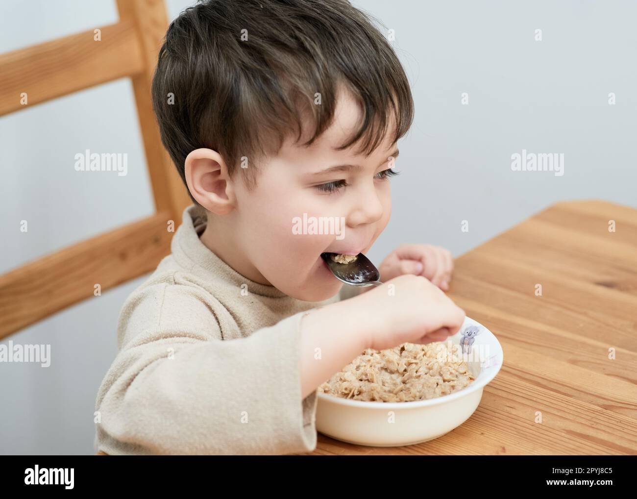 little boy eating oatmeal for breakfast in the kitchen Stock Photo - Alamy