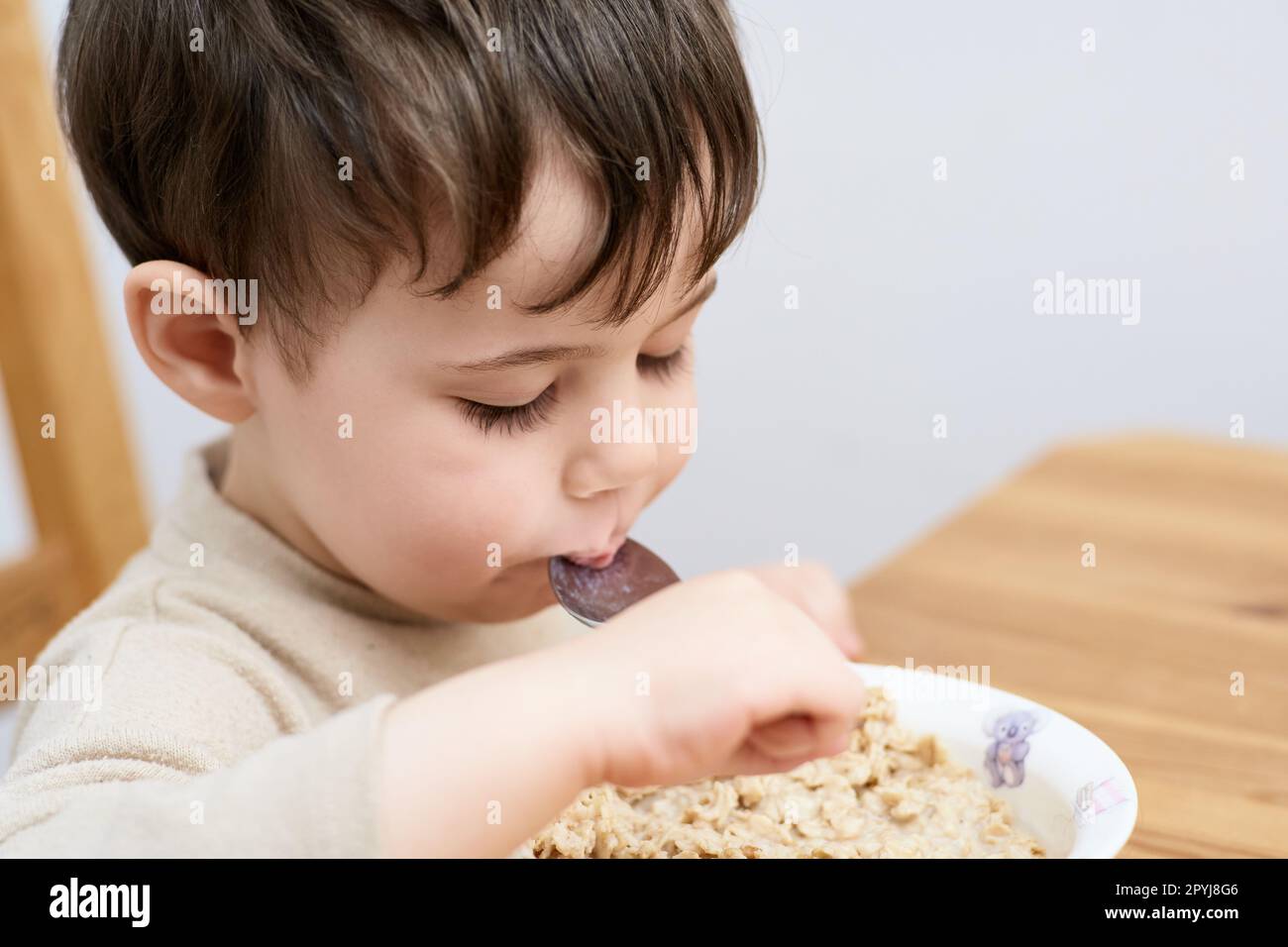 little boy eating oatmeal for breakfast in the kitchen Stock Photo - Alamy