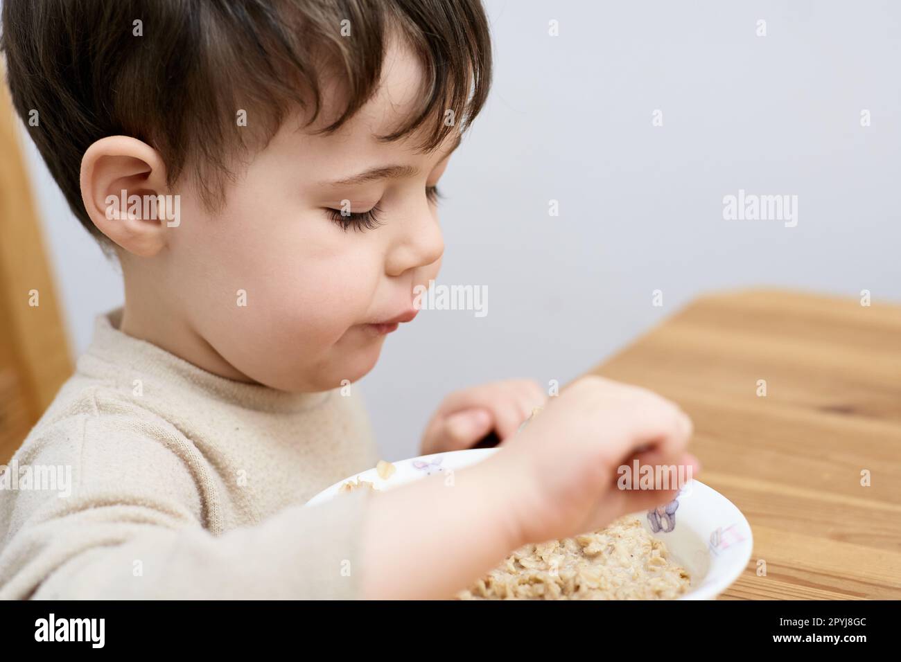 little boy eating oatmeal for breakfast in the kitchen Stock Photo - Alamy