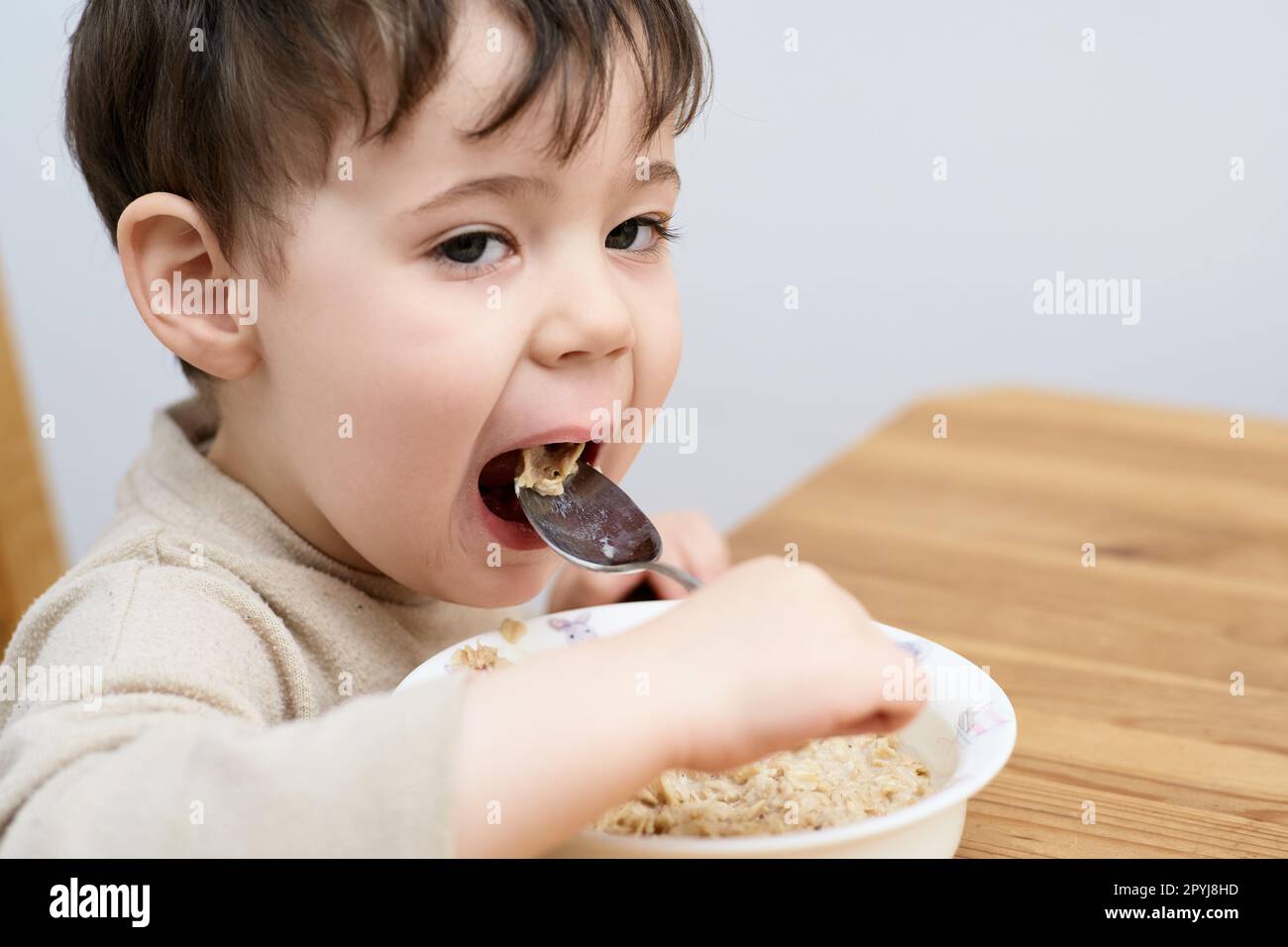 little boy eating oatmeal for breakfast in the kitchen Stock Photo - Alamy