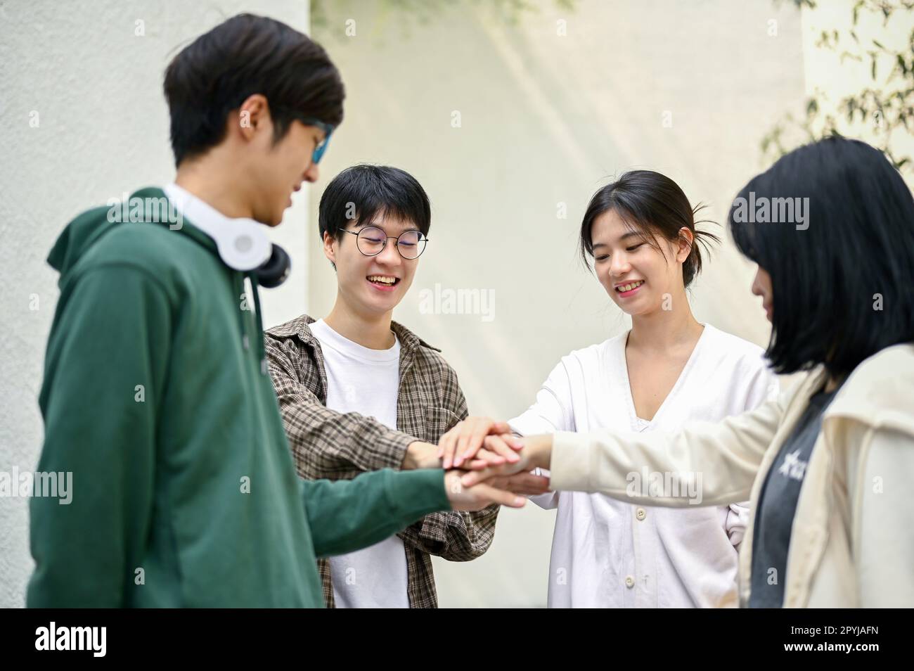 Image of a group of cheerful Asian college students putting their hands ...