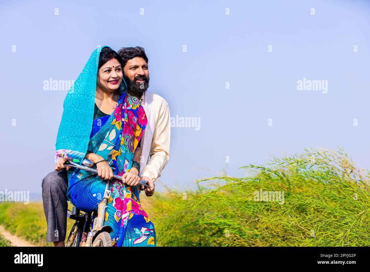 Rural Indian couple riding bicycle in agricultural field in bright ...