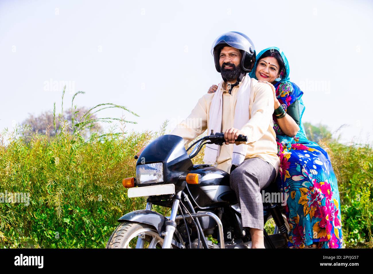 Happy young rural Indian couple wearing safety helmet riding on ...