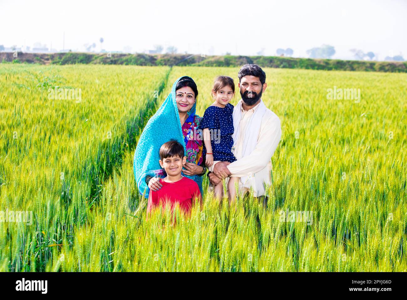 Portrait of happy young indian farmer family standing at wheat ...