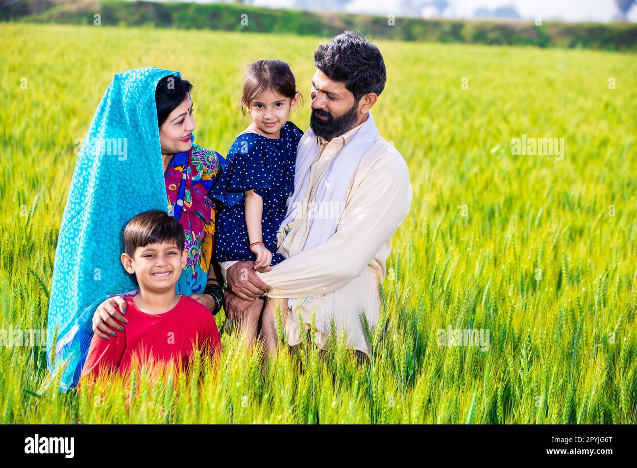 Portrait of happy young indian farmer family standing at wheat ...