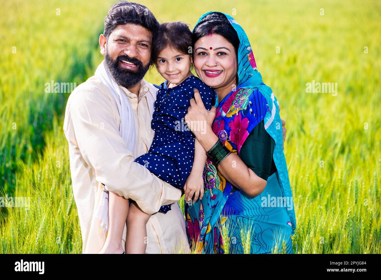 Portrait of happy young indian farmer family standing at wheat ...