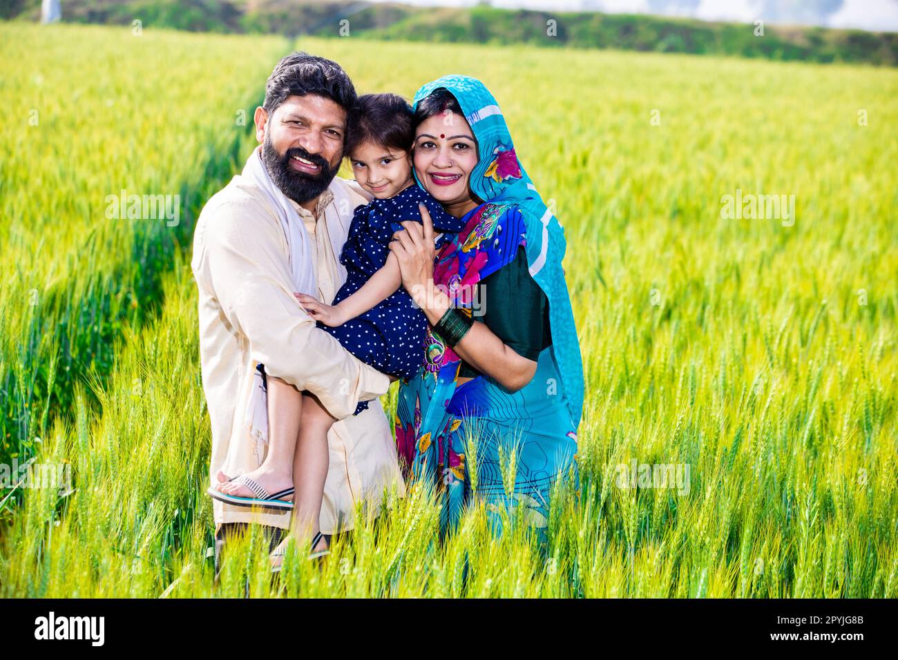 Portrait of happy young indian farmer family standing at wheat ...